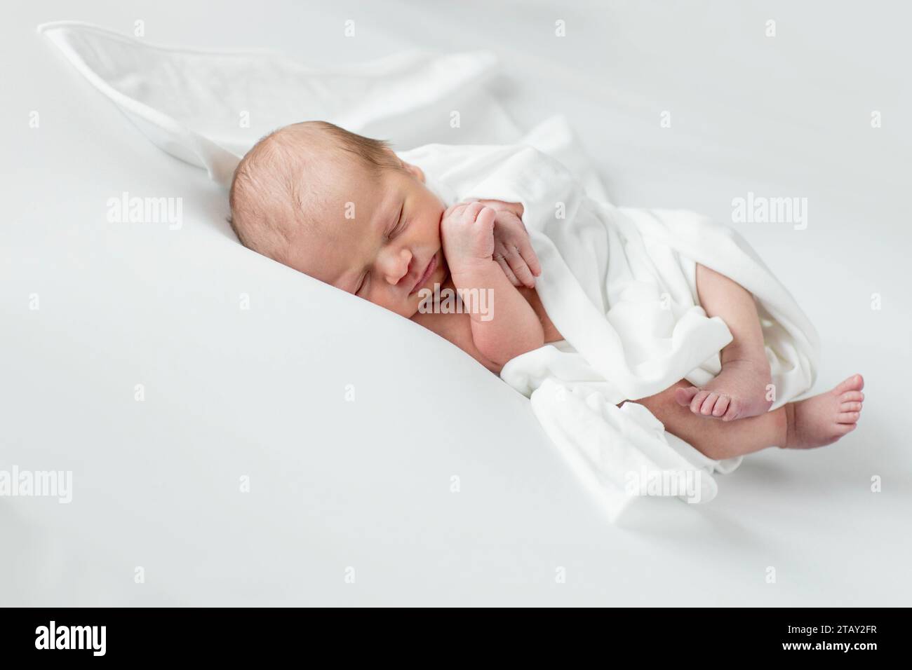 A 3-day-old baby wrapped in white cloth sleeping on a white background ...
