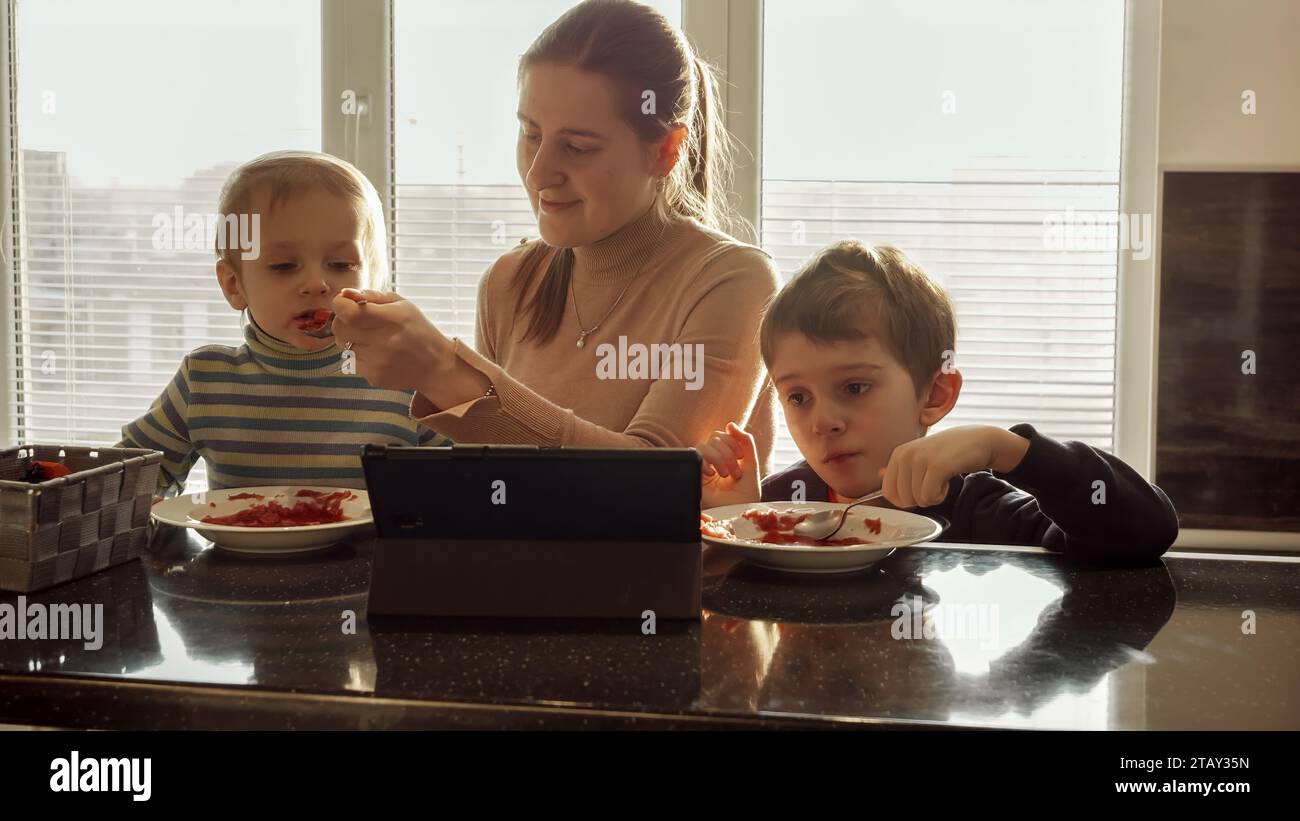 Caring mother giving soup to her children on dinner. Domestic food ...