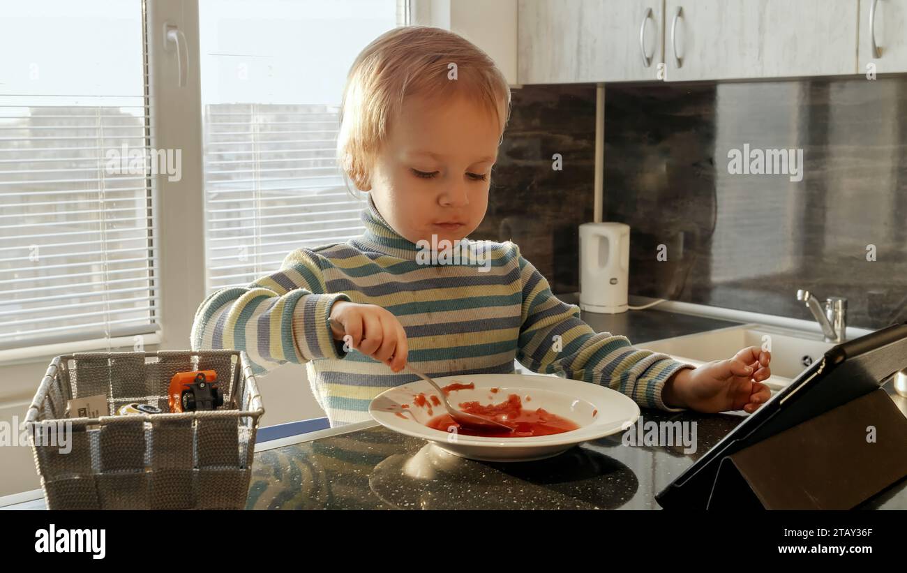 Little boy eating soup and watching video on tablet computer. Domestic ...