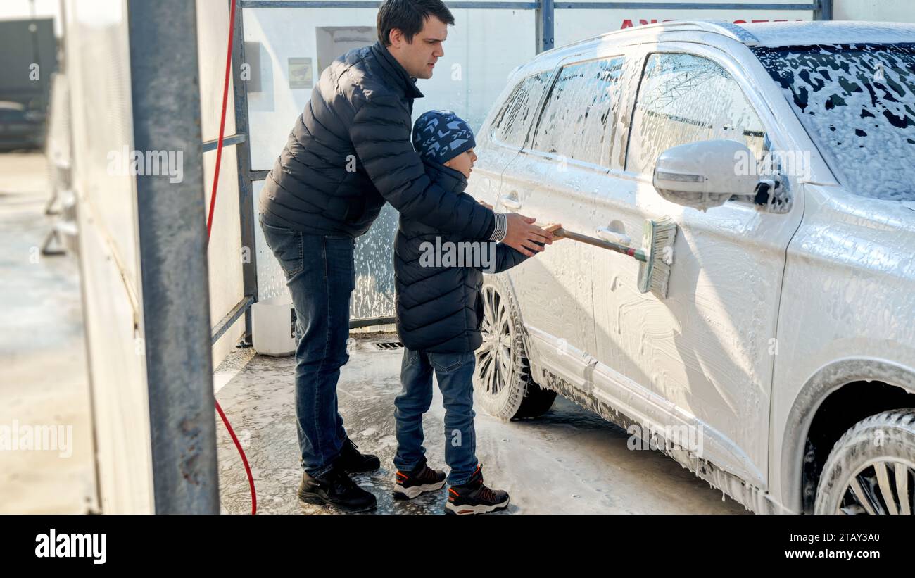 Young smiling man with son washing car outdoors with brush and foam ...