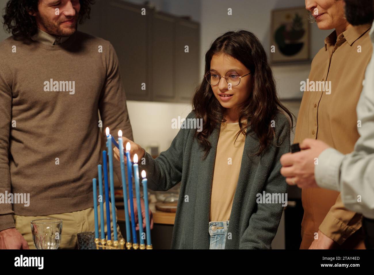 Pretty pre-teen girl lighting blue candles of menorah while standing ...