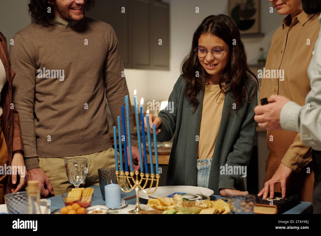 Cute smiling girl from Jewish family lighting menorah candles while ...