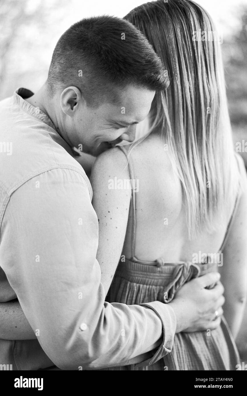 Smiling guy hugs girl by the waist and kisses her shoulder. Back view ...