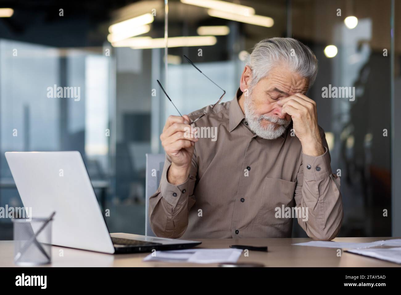 Tired and overworked senior gray-haired man working overtime in office ...