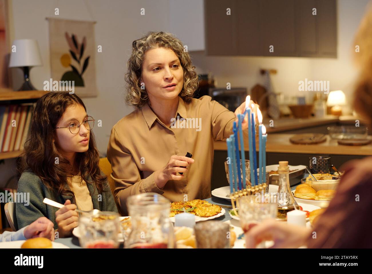 Mature Jewish woman lighting candles on menorah candlestick by served ...