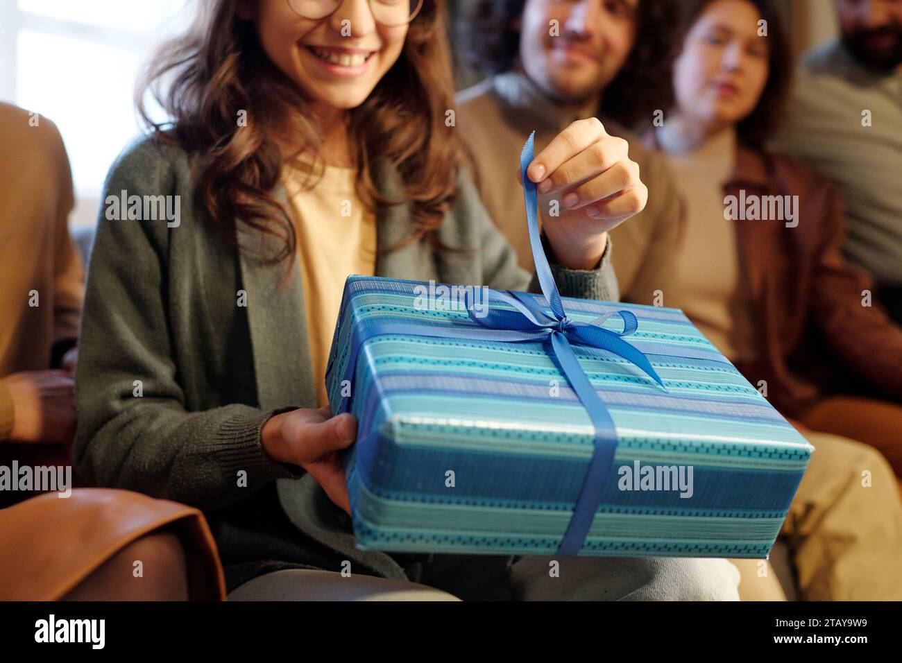 Blue packed giftbox in hands of cute girl pulling silk ribbon on top ...