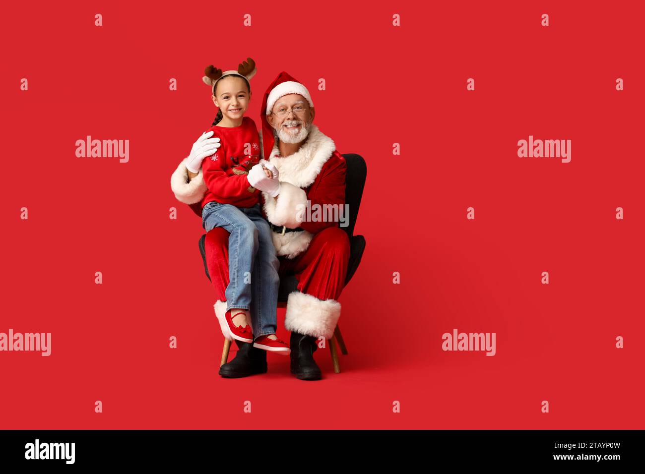 Santa Claus and cute little girl sitting on armchair against red ...