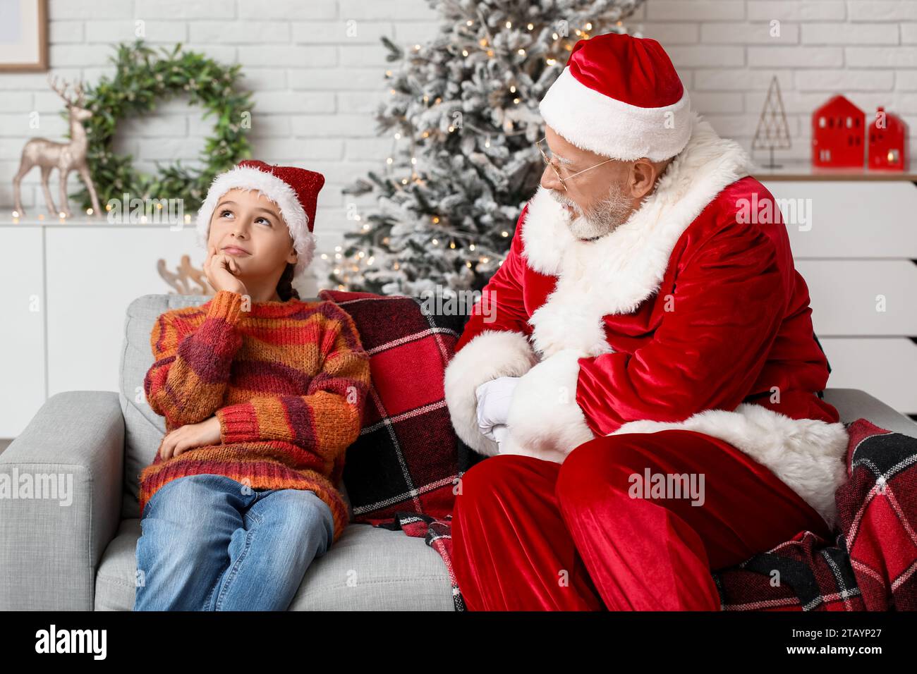 Santa Claus and thoughtful little girl sitting on sofa in decorated ...