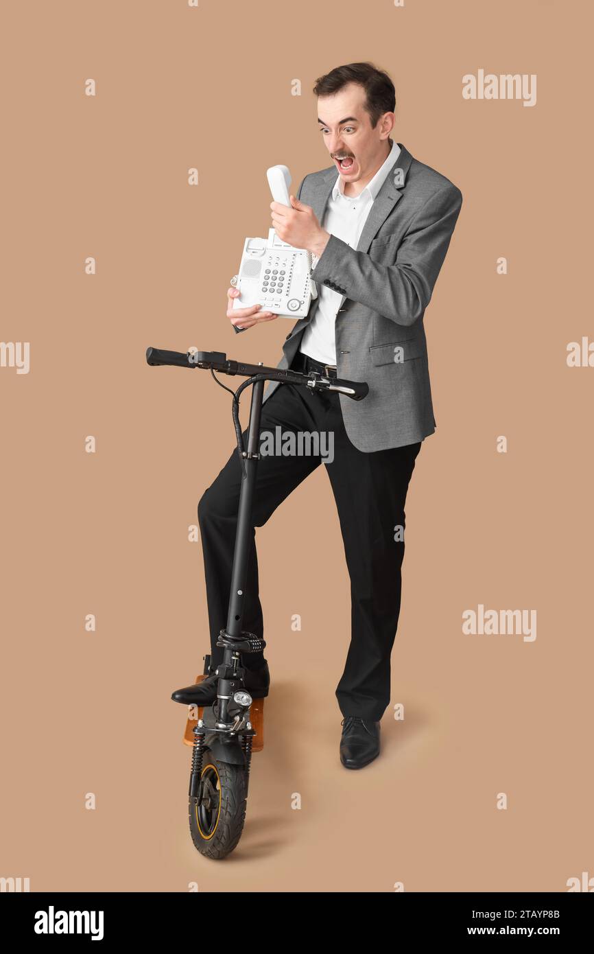Portrait of angry businessman with kick scooter and phone on beige ...