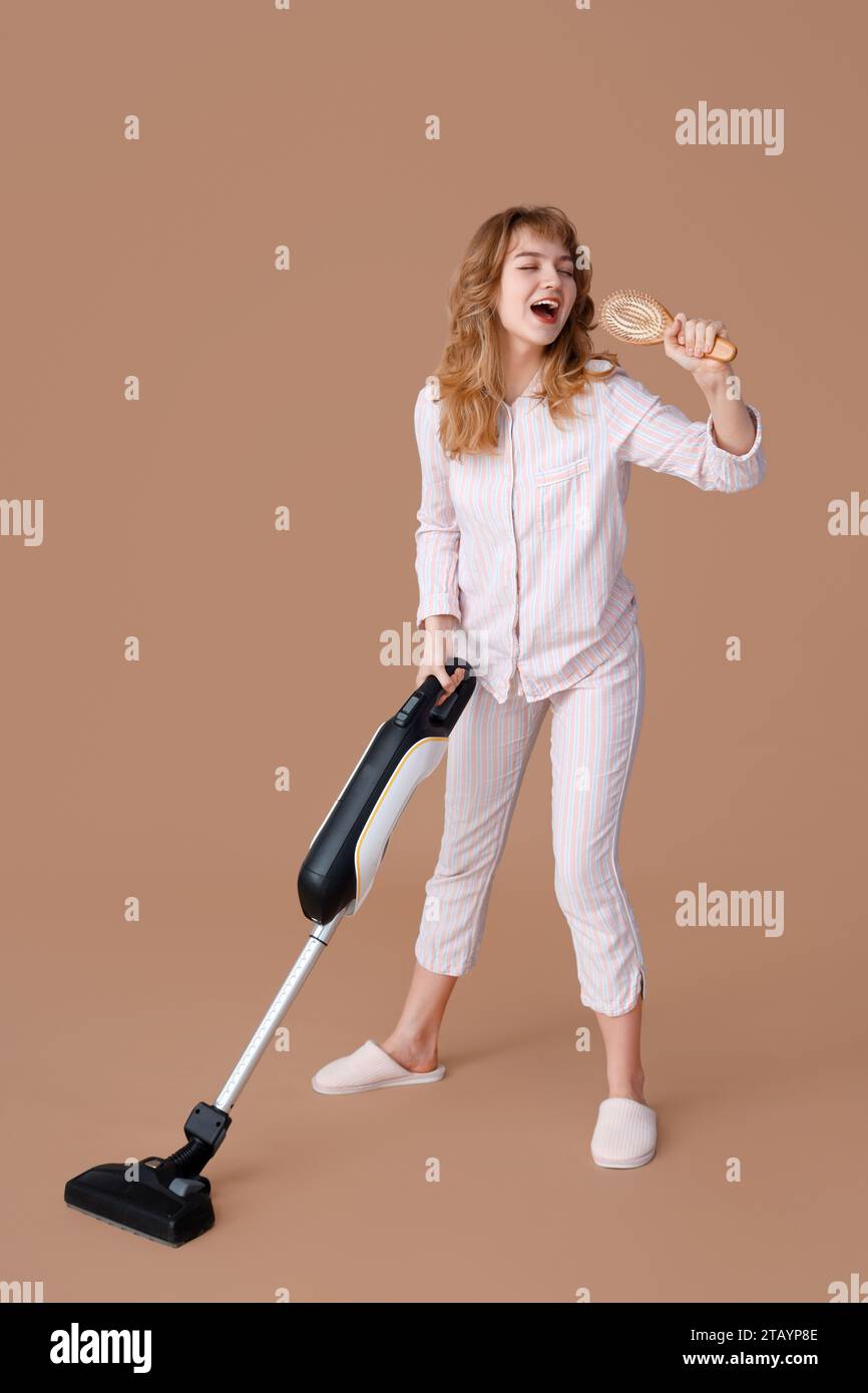Portrait of pretty young woman in pajamas singing with hairbrush while ...