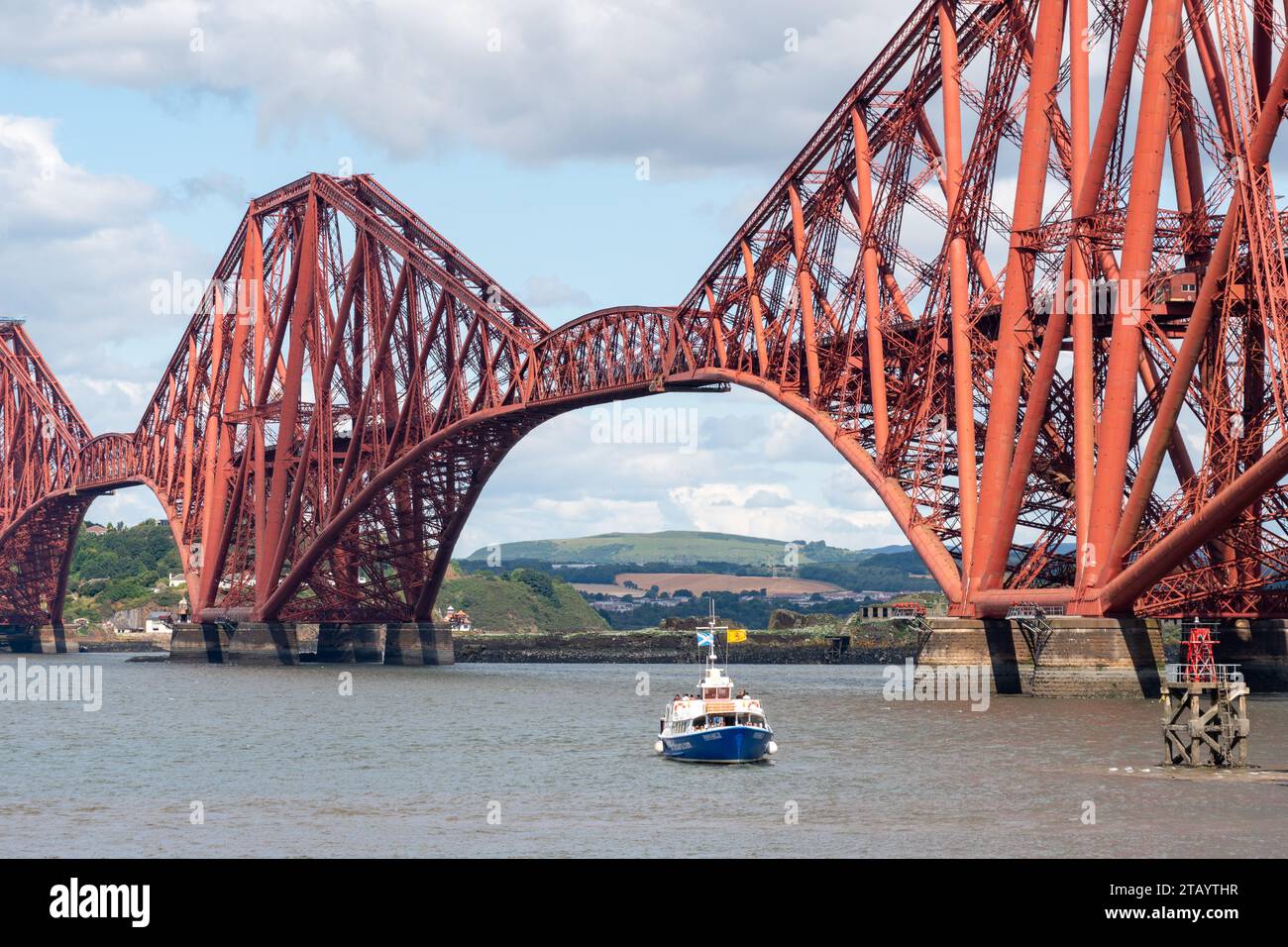 A small ferry boat next to the famous Forth Bridge in Queensberry Stock ...