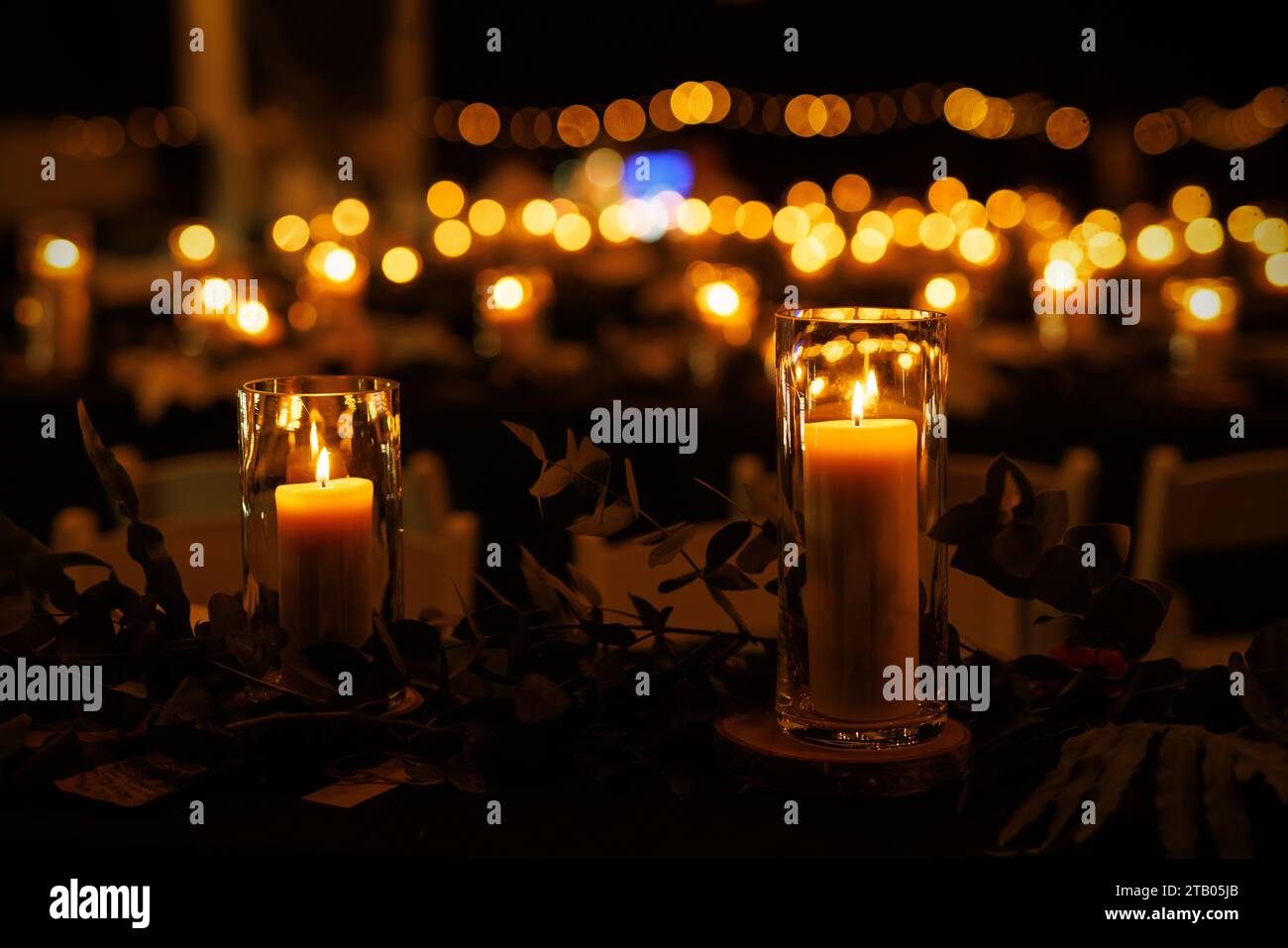 A romantic table setting with lit candles and greenery at a nighttime ...