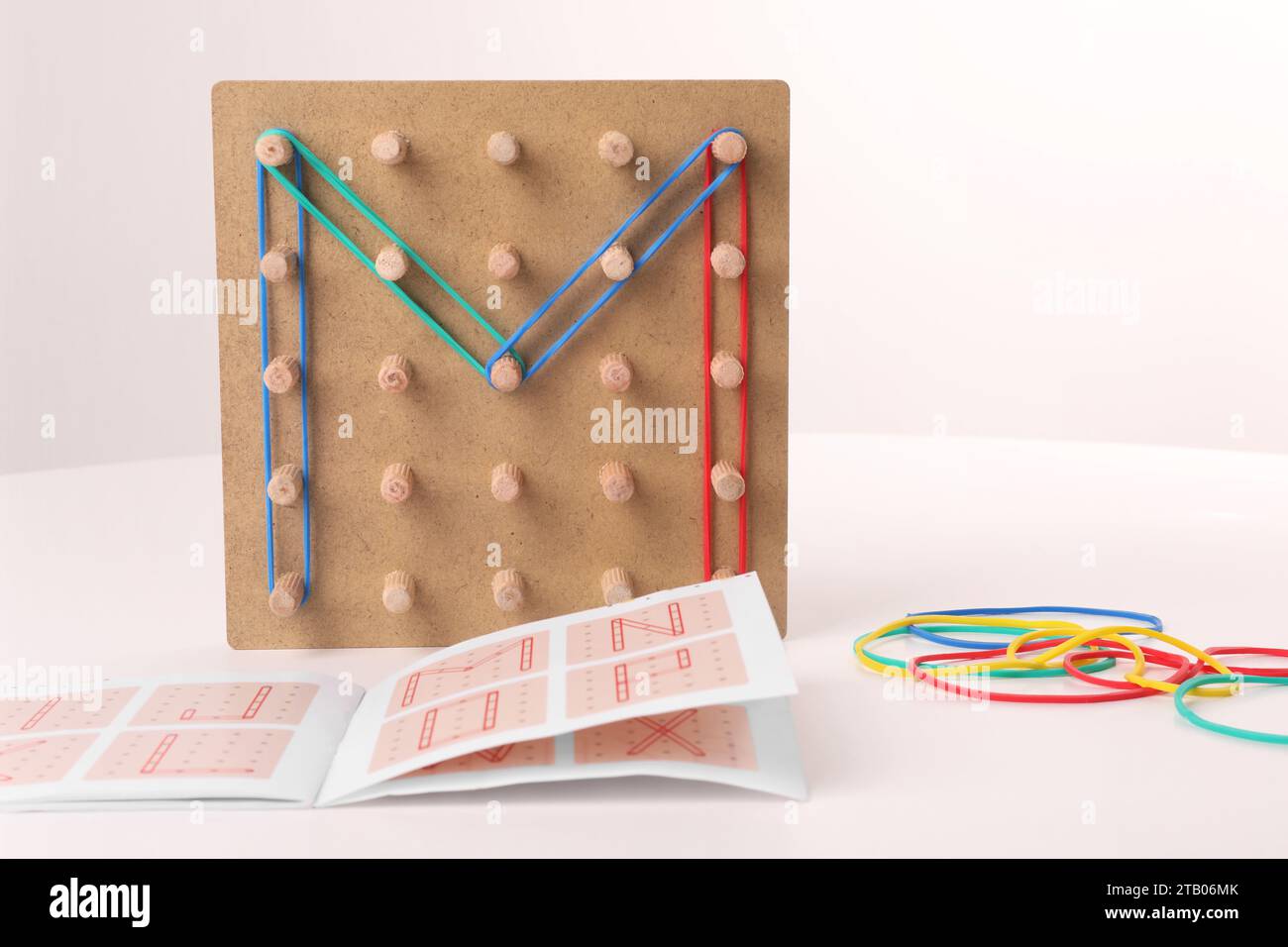 Wooden geoboard with letter M made of rubber bands and instruction on ...