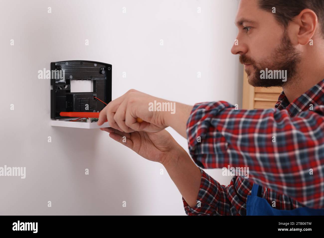 Technician installing home security alarm system on white wall indoors ...