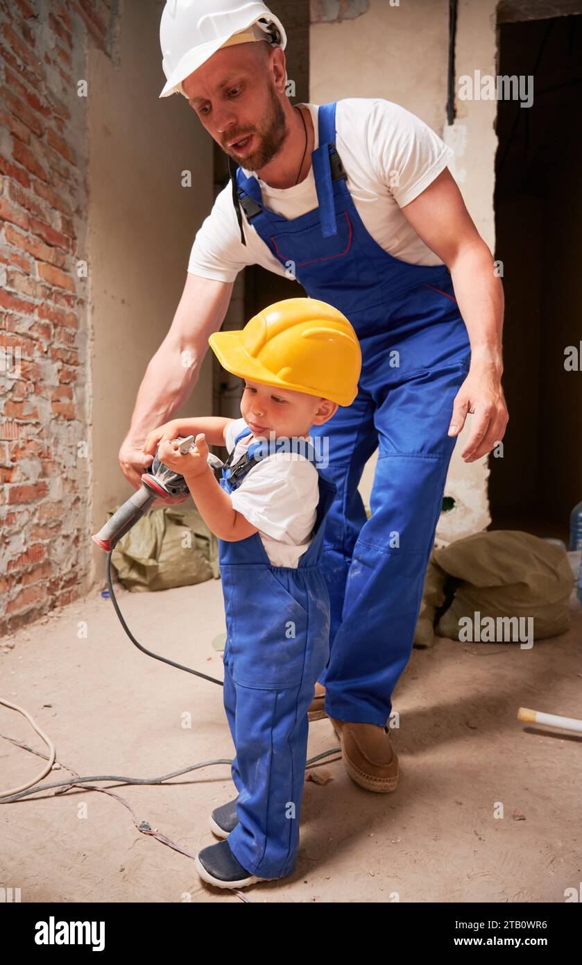 Male builder crouching down and holding electric hammer drill while ...