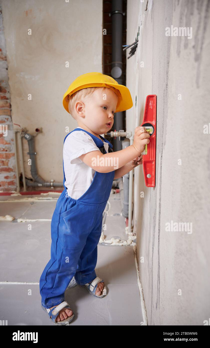 Child construction worker checking wall surface with spirit level tool ...