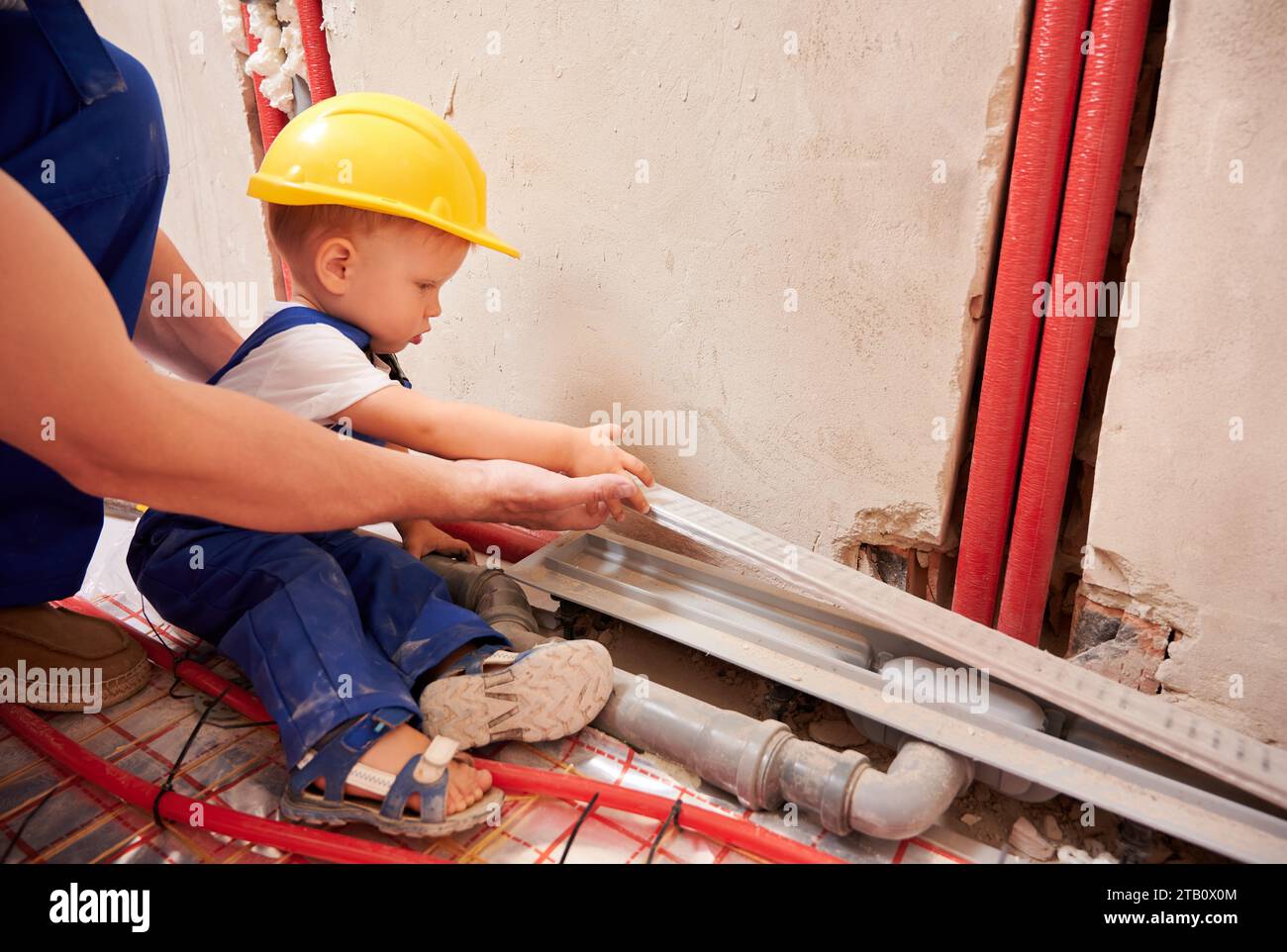 Man and little boy sitting by the wall with pipes and holding material ...