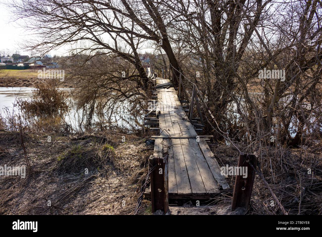 An old damaged pedestrian bridge in a village, spanning a river and ...