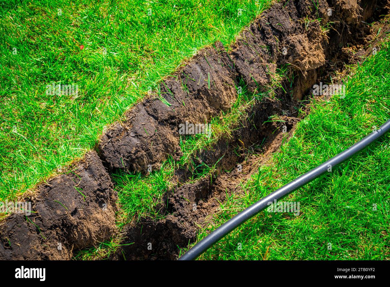 A ditch dug in the lawn for laying a plastic pipe. Removed top layer of ...