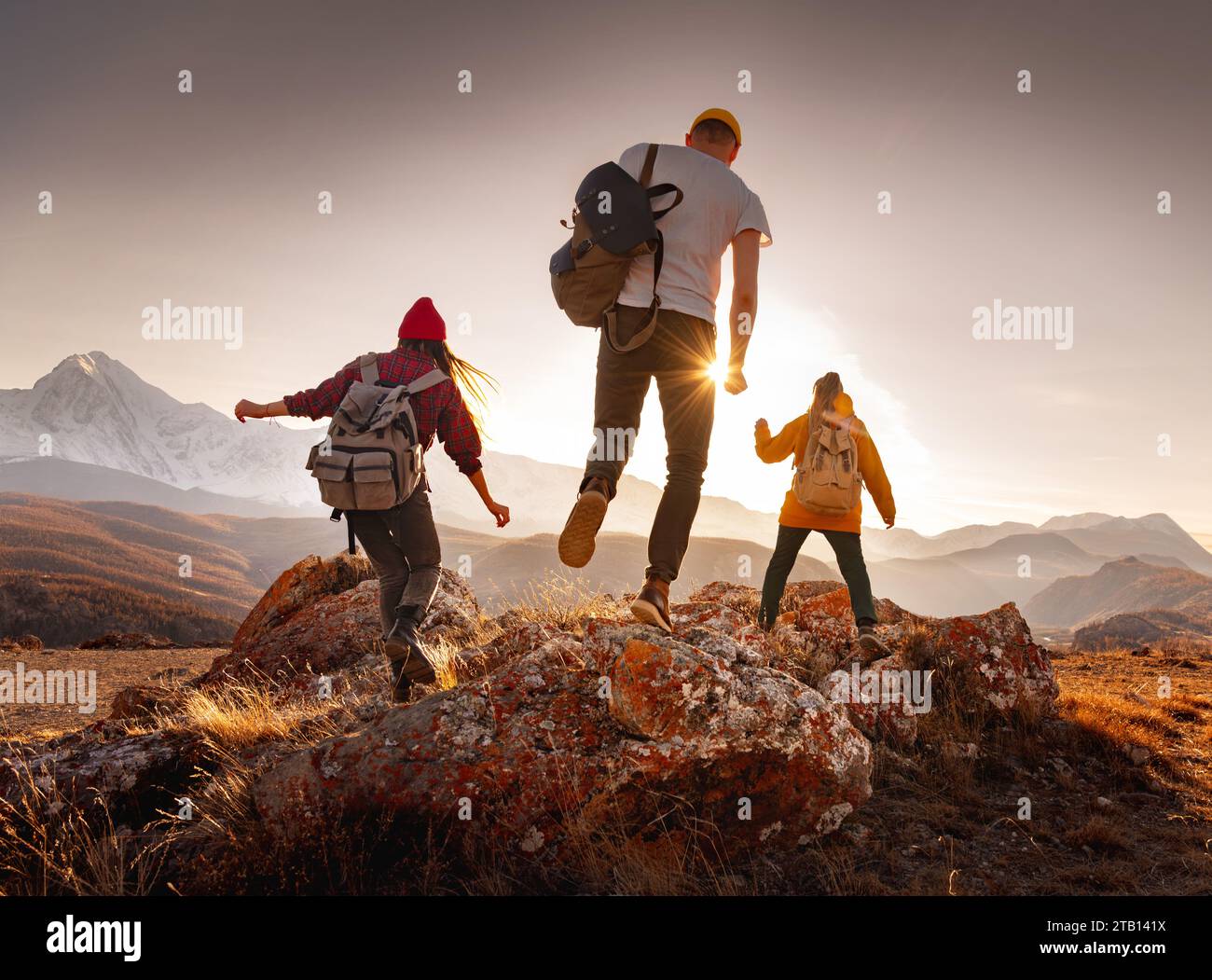 Three young hikers with small backpacks walks at sunset mountains ...
