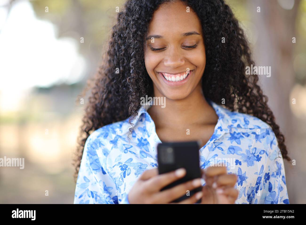 Front view portrait of a happy black woman using phone in a park Stock Photo - Alamy