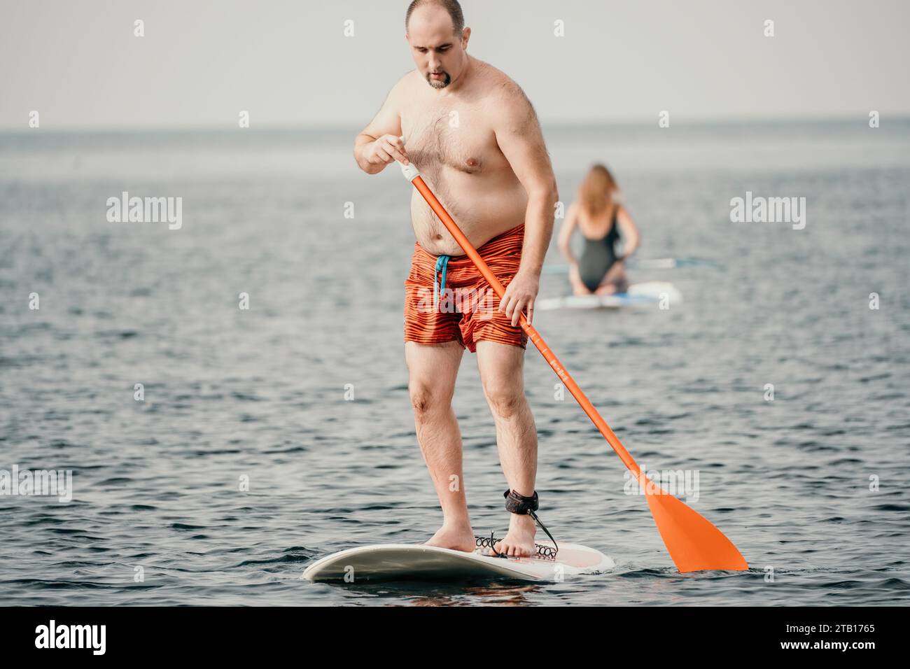 Active mature male paddler with his paddleboard and paddle on a sea at summer. Happy senior man ...