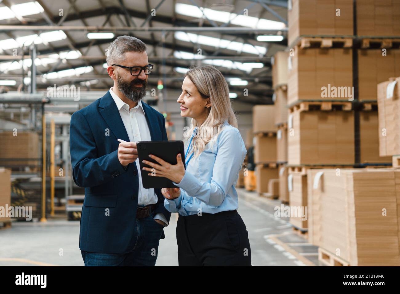 Female warehouse manager talking with logistics employee in warehouse ...