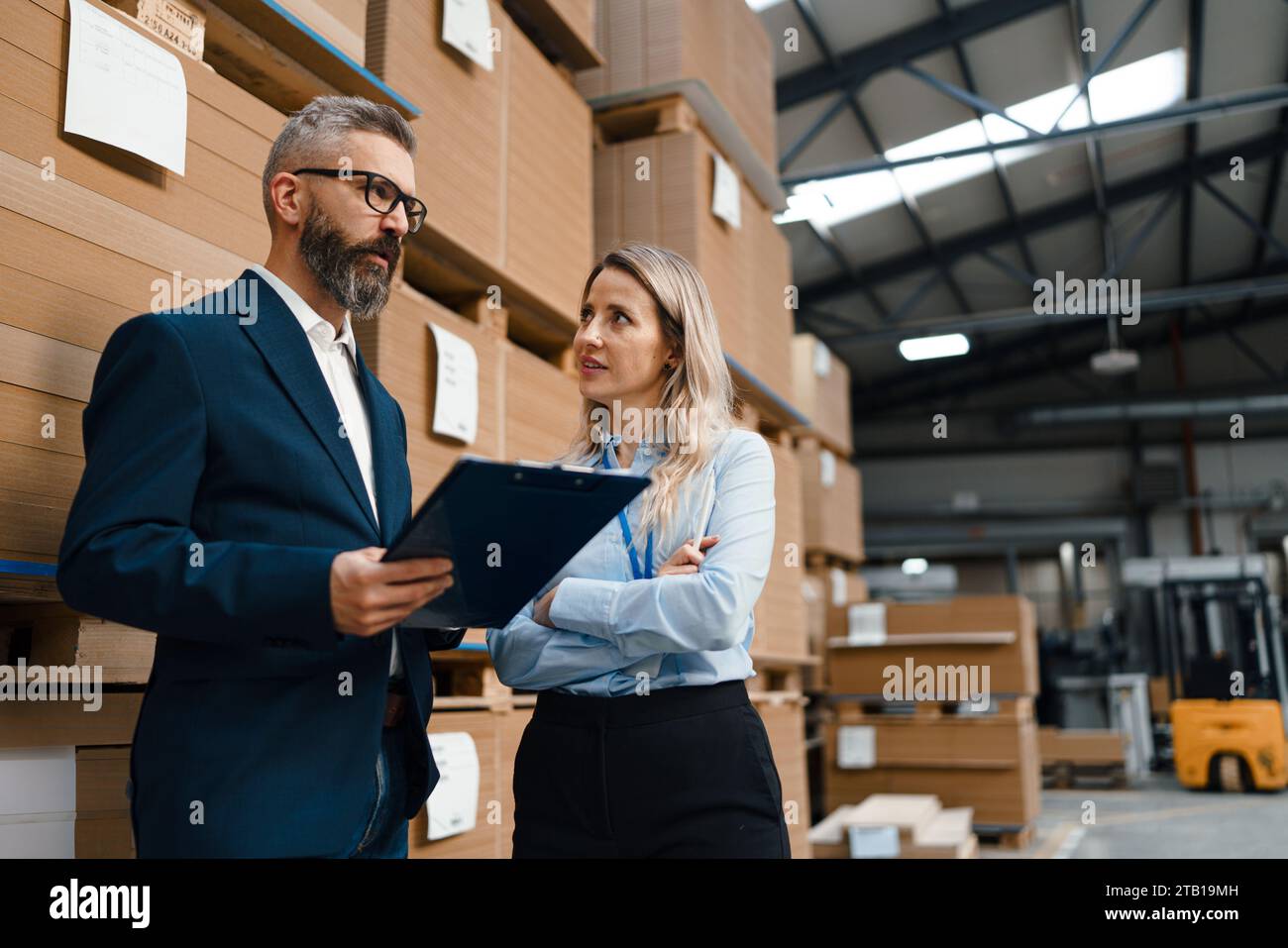 Female warehouse manager talking with logistics employee in warehouse ...