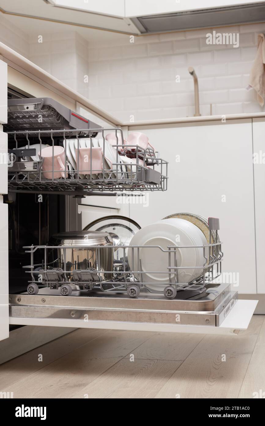 Open built-in dishwasher machine with clean cutlery, dishes, plates in ...