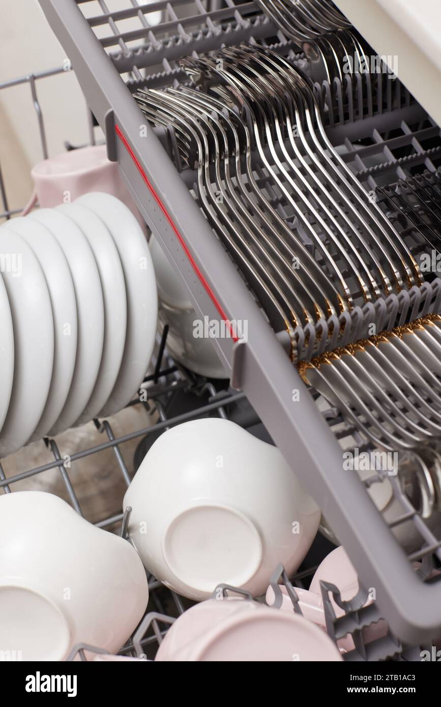 Open built-in dishwasher machine with clean cutlery, dishes, plates in ...
