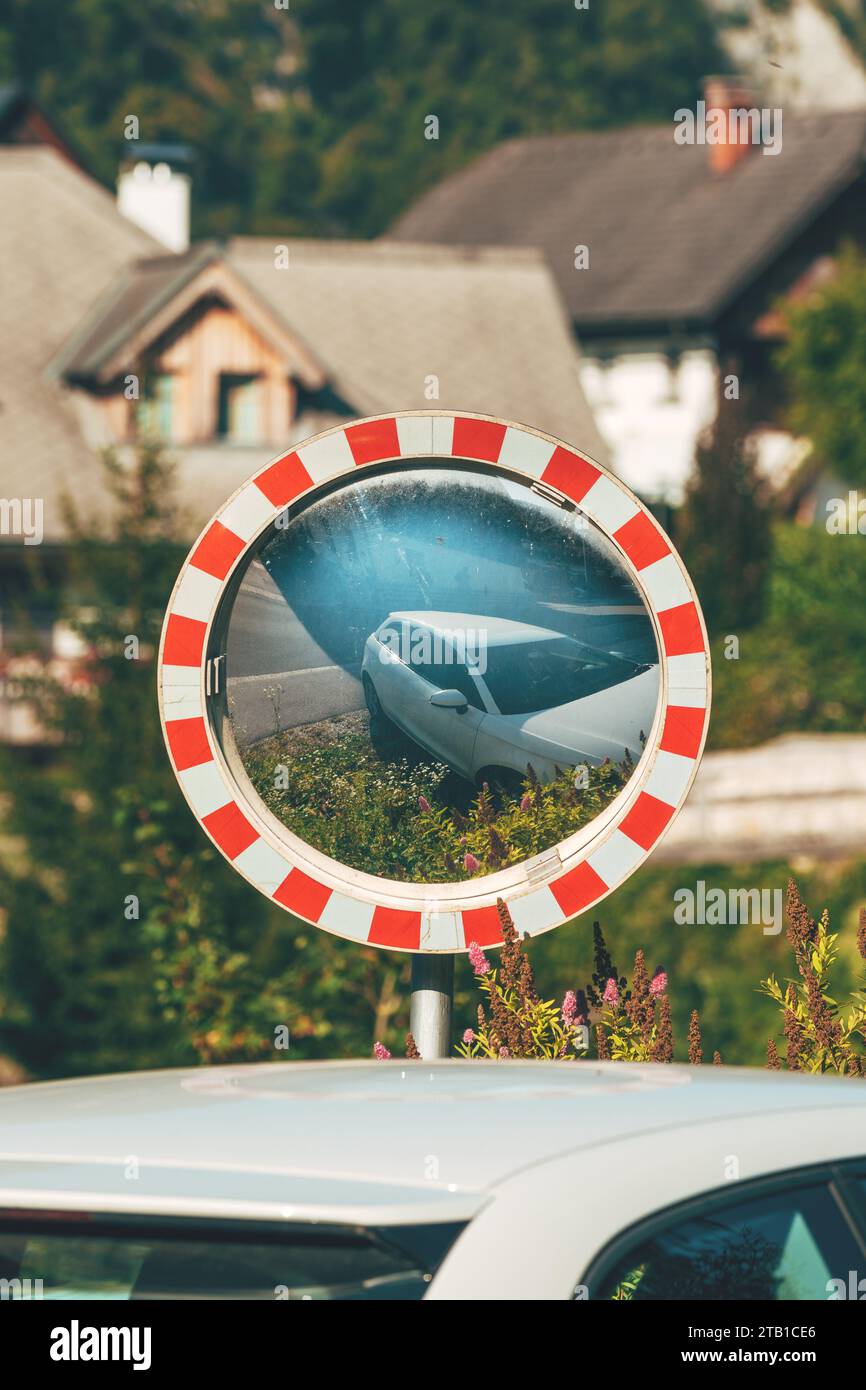 Traffic mirror with a reflection of white car in scenic alpine village ...