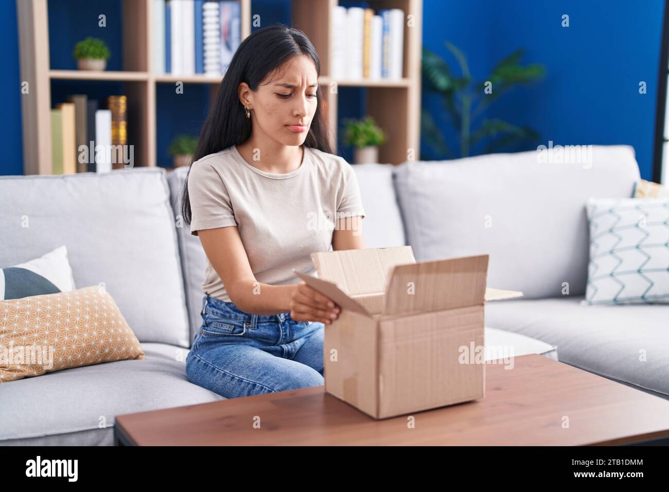 Young hispanic woman opening cardboard box clueless and confused ...