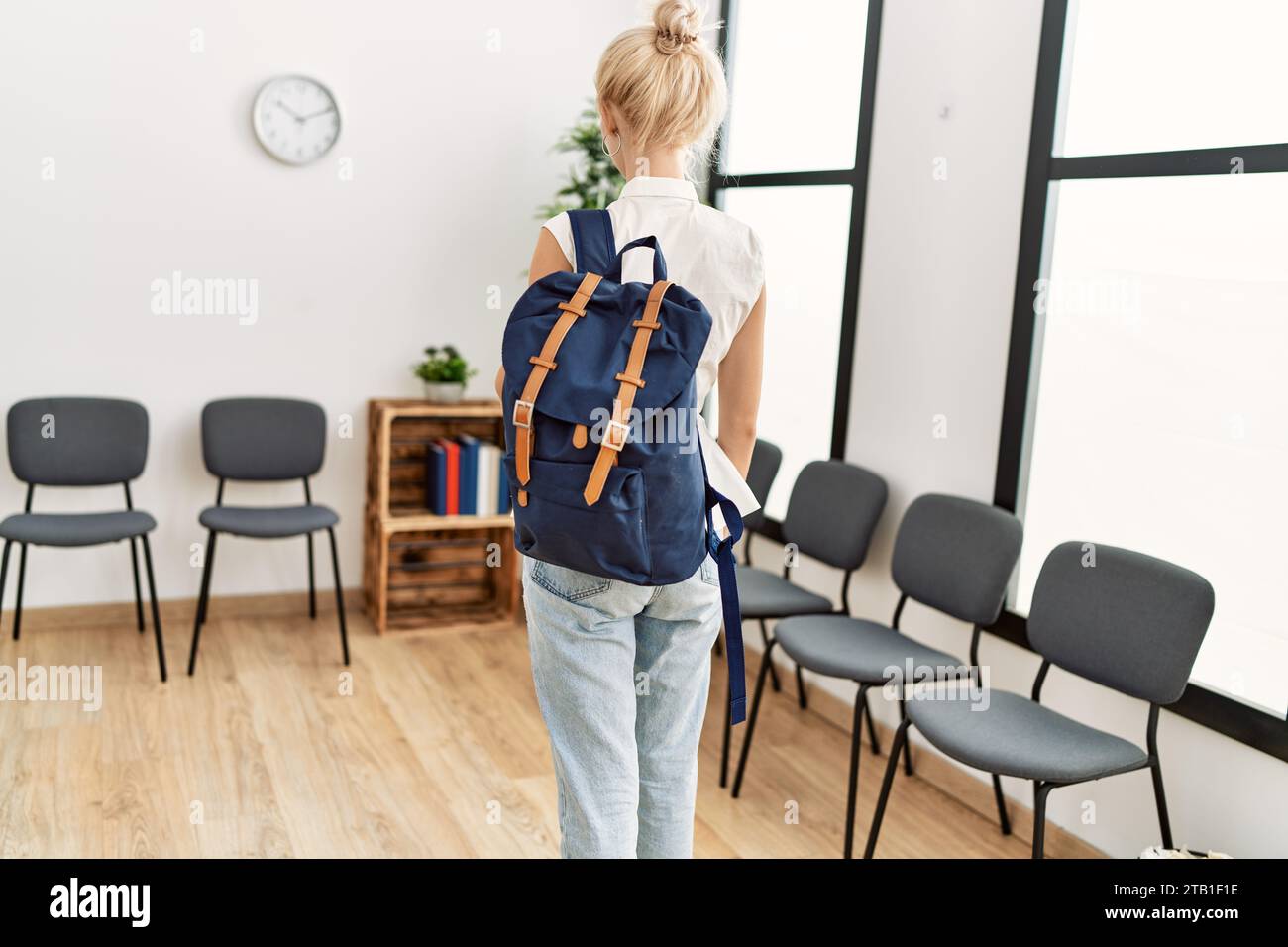 Young blonde woman standing backwards looking clock at waiting room ...