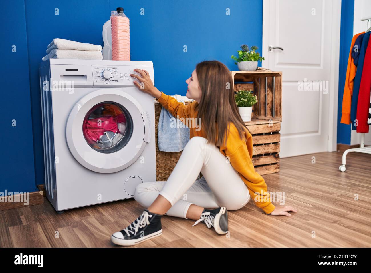 Young blonde woman sitting on floor turning washing machine on at ...