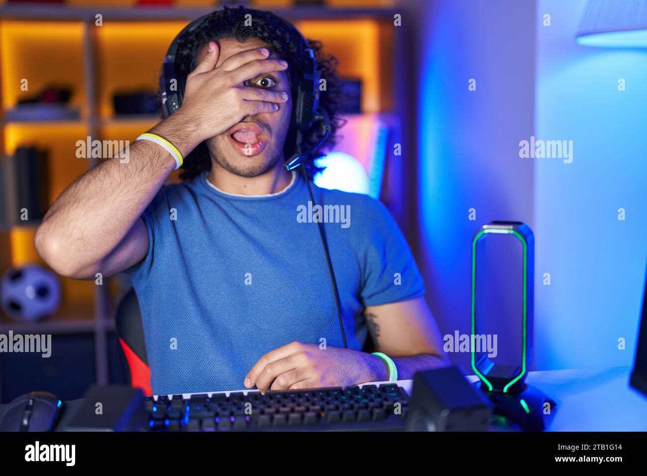 Hispanic man with curly hair playing video games peeking in shock ...