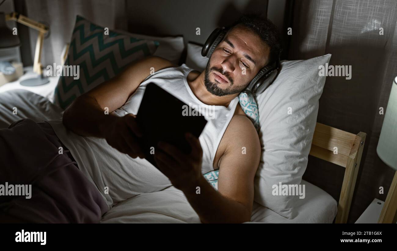 Young arab man using touchpad lying on the bed wearing headphones at bedroom Stock Photo - Alamy