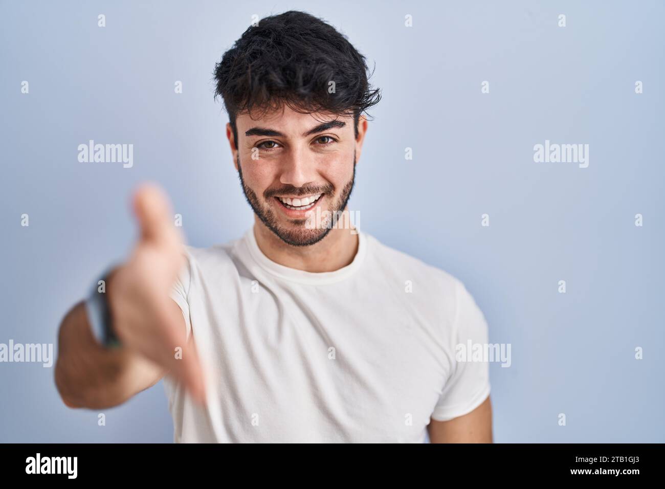 Hispanic man with beard standing over white background smiling friendly ...