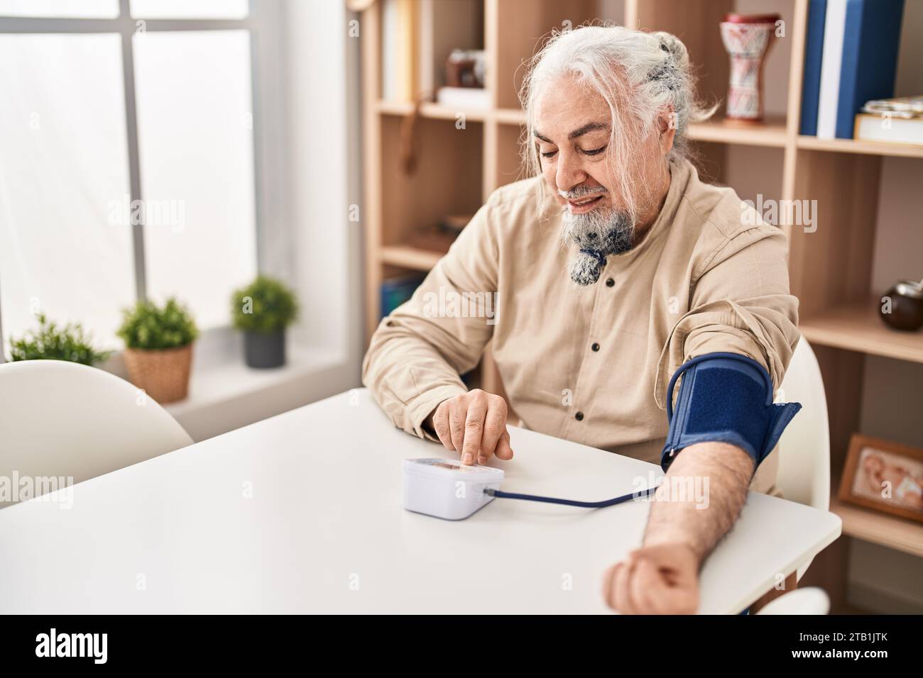 Middle age grey-haired man measuring pulse using tensiometer at home ...