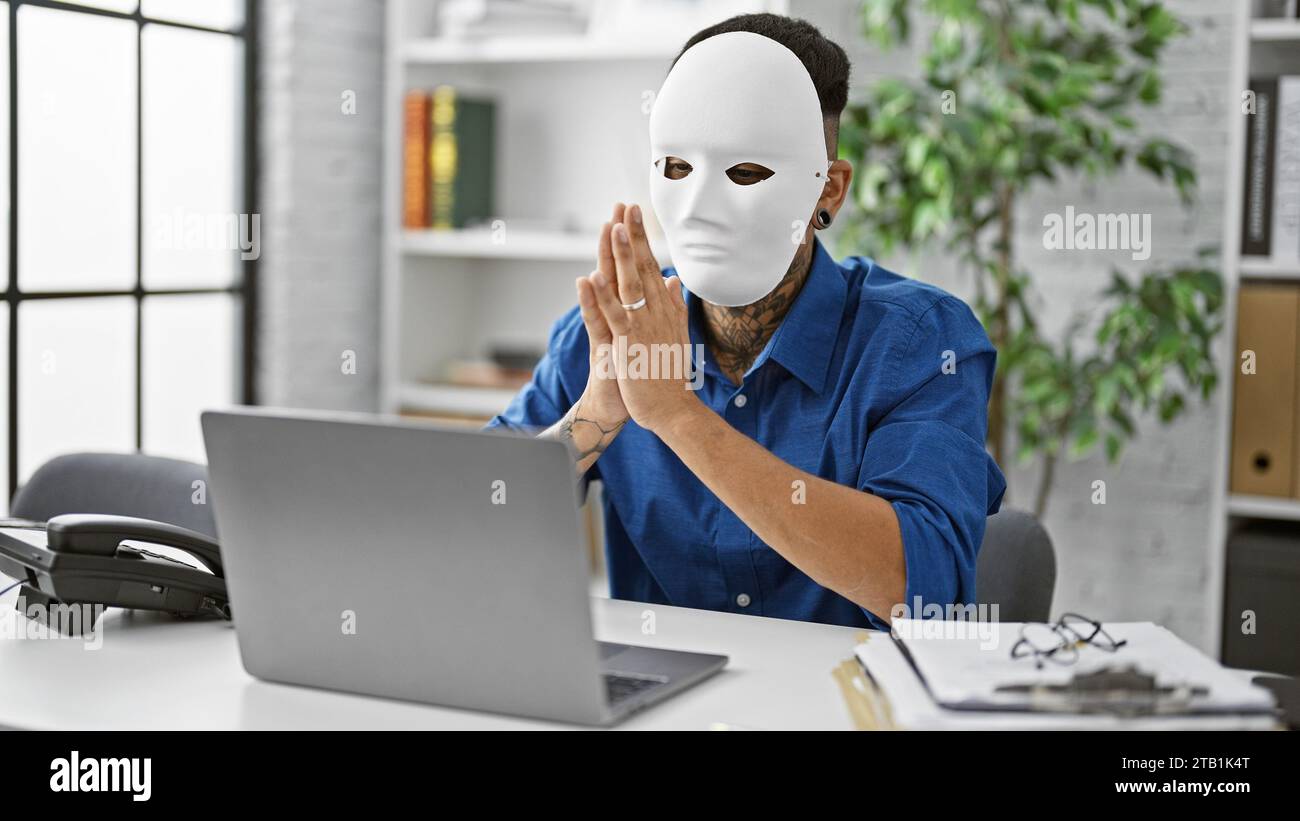 Young latin man hacking, a masked hacker tapping away on his laptop ...