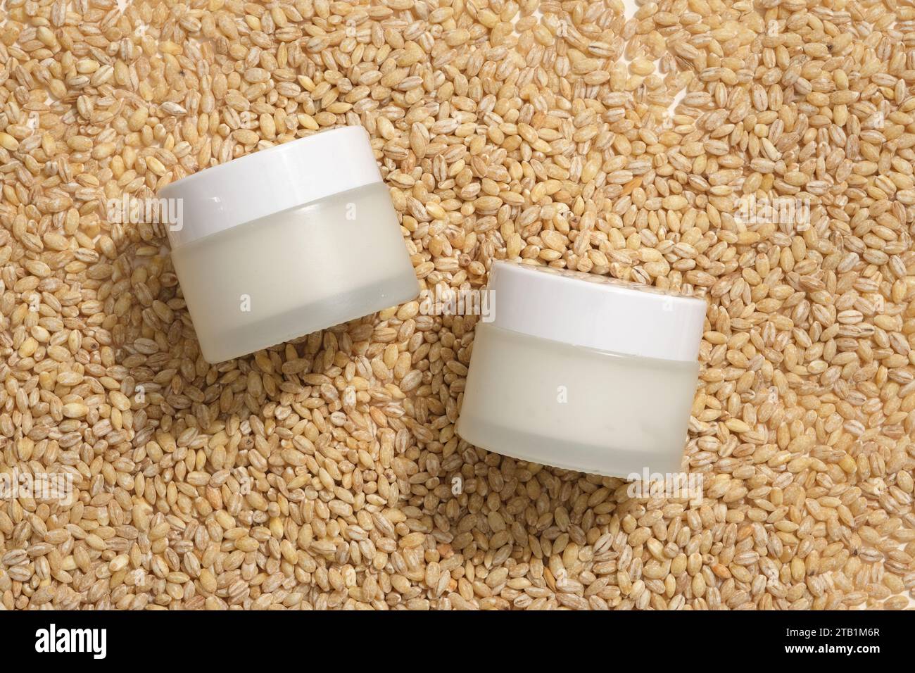 Cosmetic jars with empty label placed on a pile of wheat seeds. Flat ...