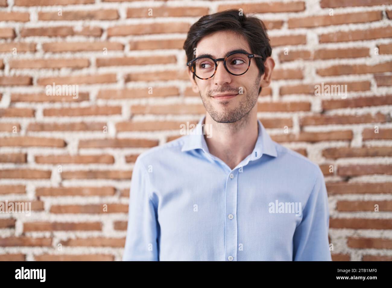 Young hispanic man standing over brick wall background smiling looking ...