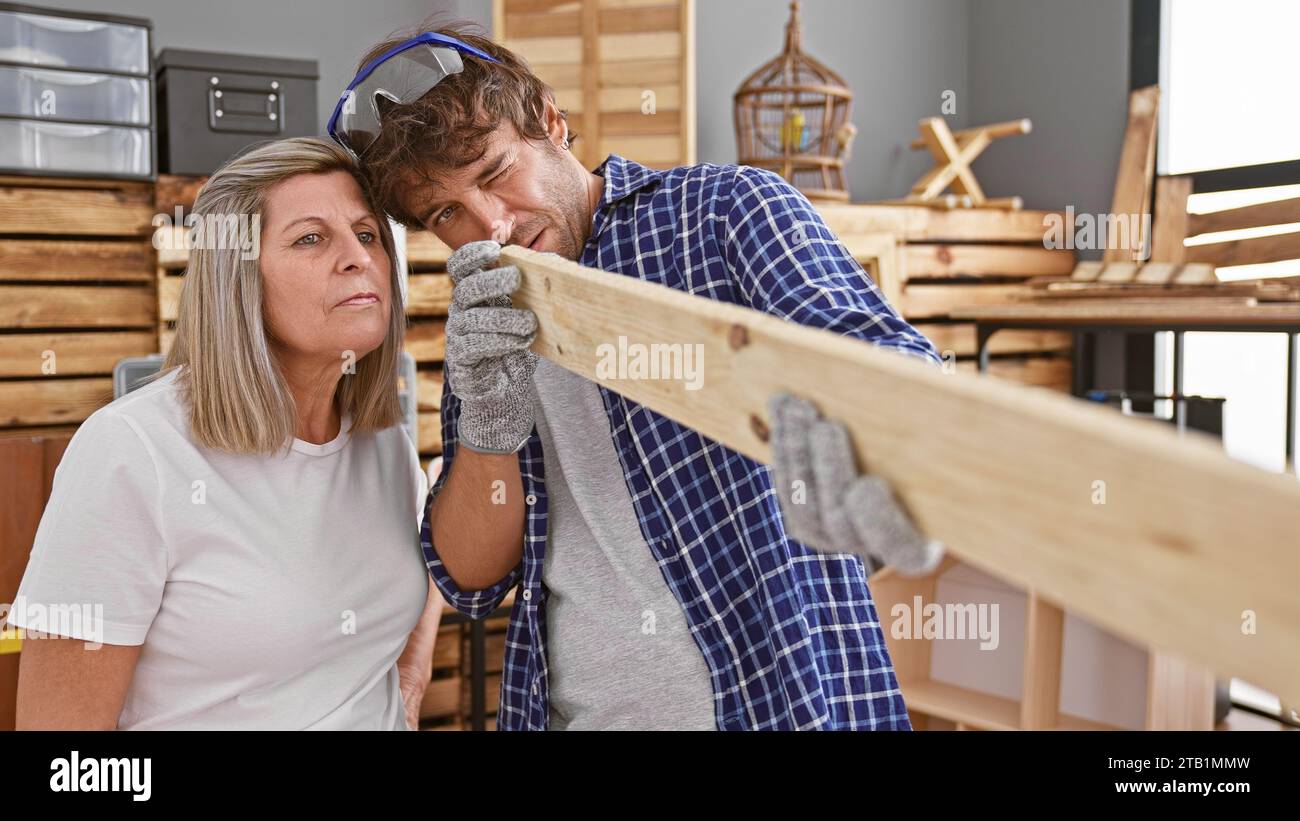 Two pro carpenters, man and woman, together looking at timber plank, giving a thumbs-up gesture ...