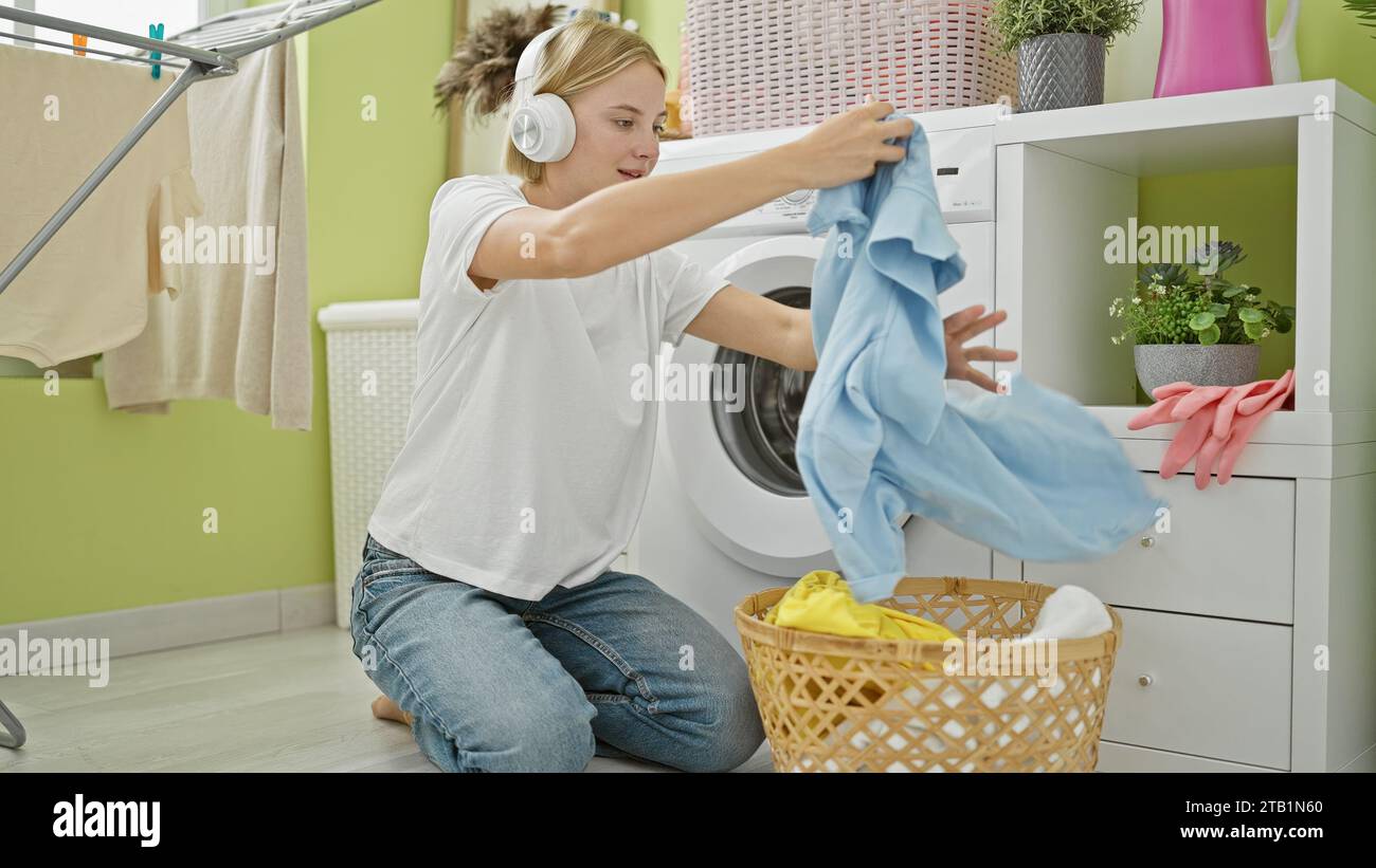 Young blonde woman listening to music holding clothes of basket at ...