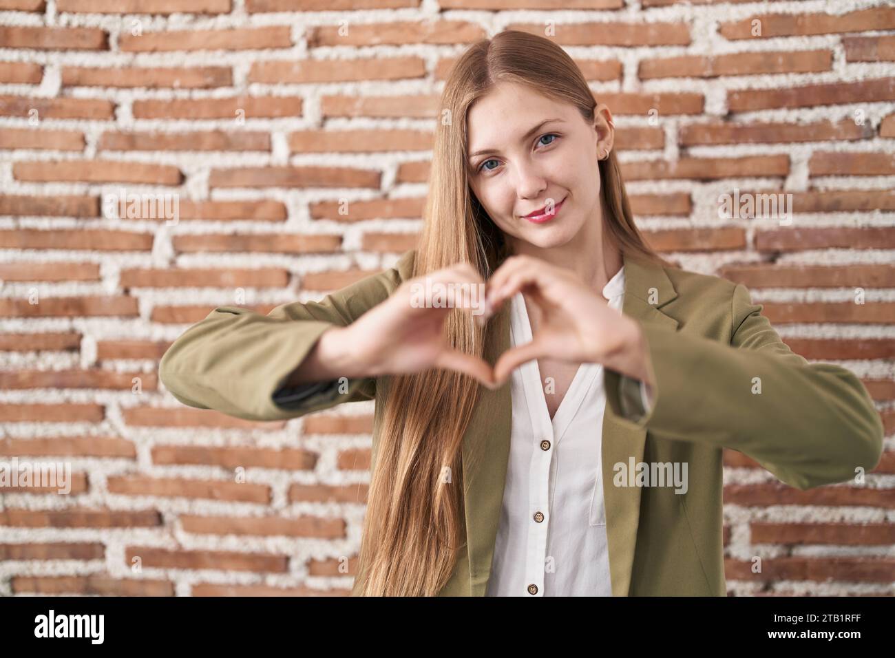 Young caucasian woman standing over bricks wall background smiling in ...