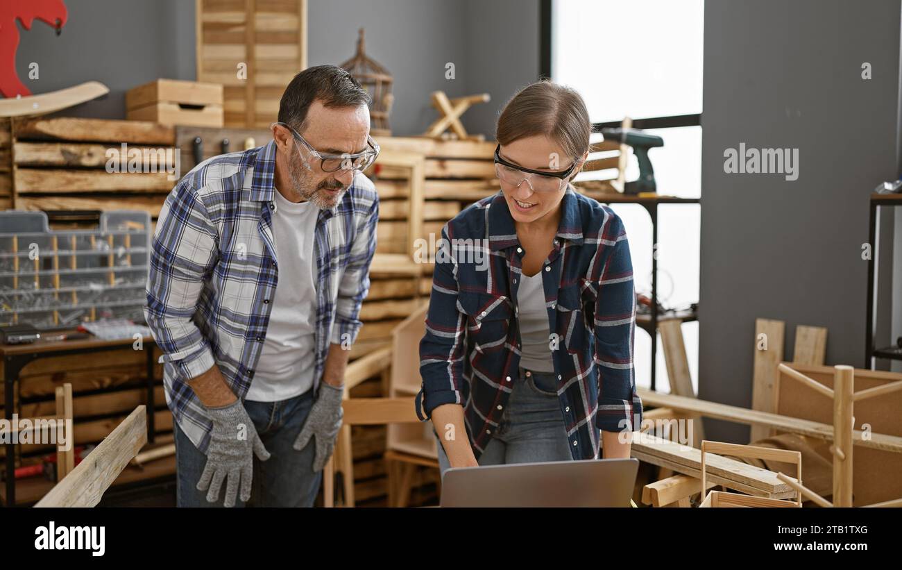 Two skillful carpenters, man and woman connecting online on laptop amid sawdust and timbers at ...