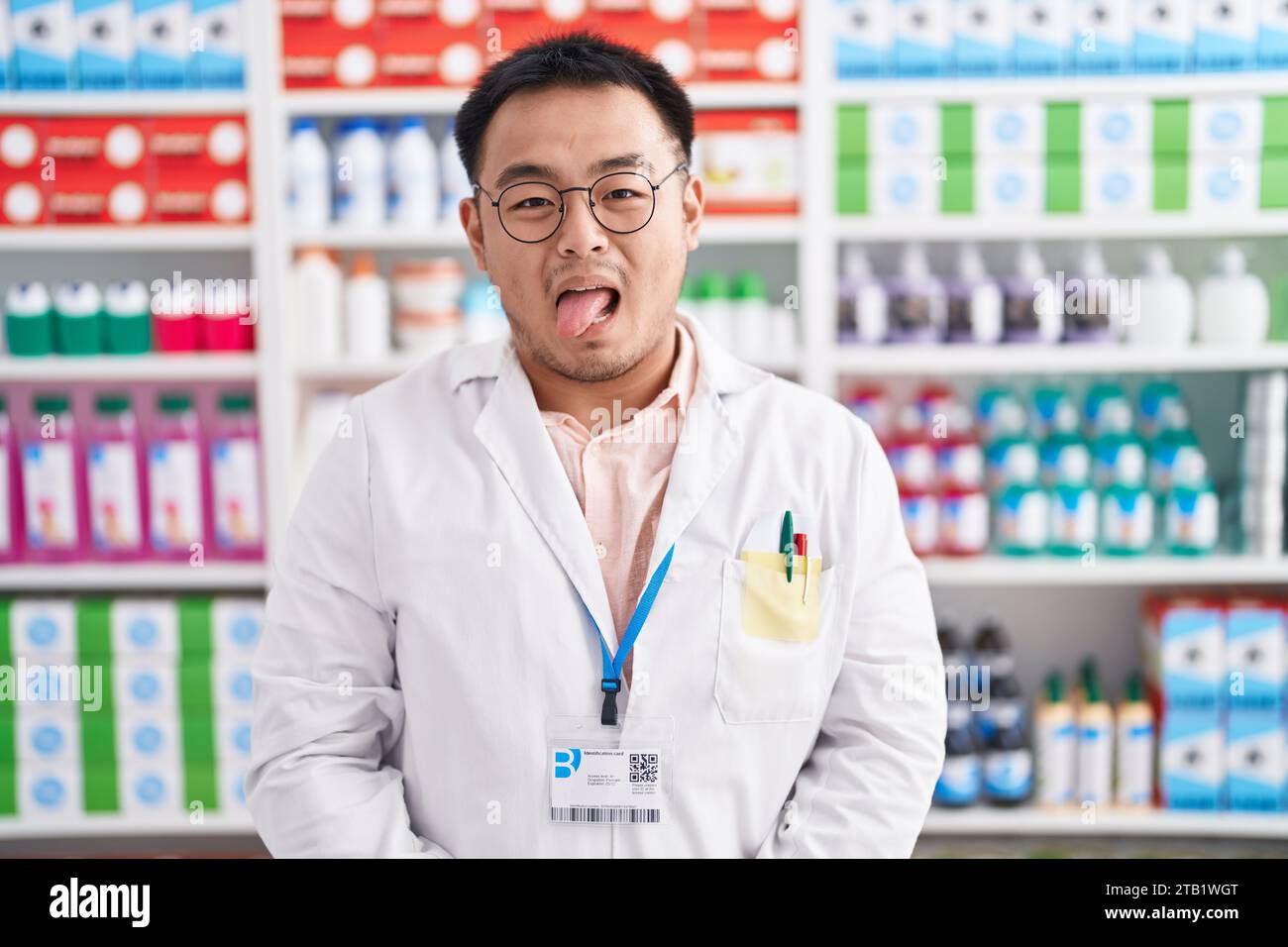 Chinese young man working at pharmacy drugstore sticking tongue out ...