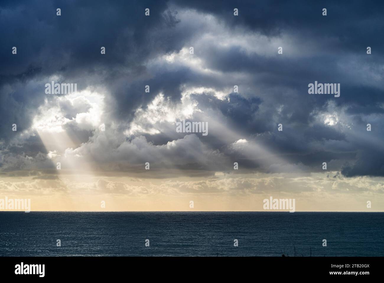 Rays of sun shining through storm clouds onto ocean Stock Photo - Alamy
