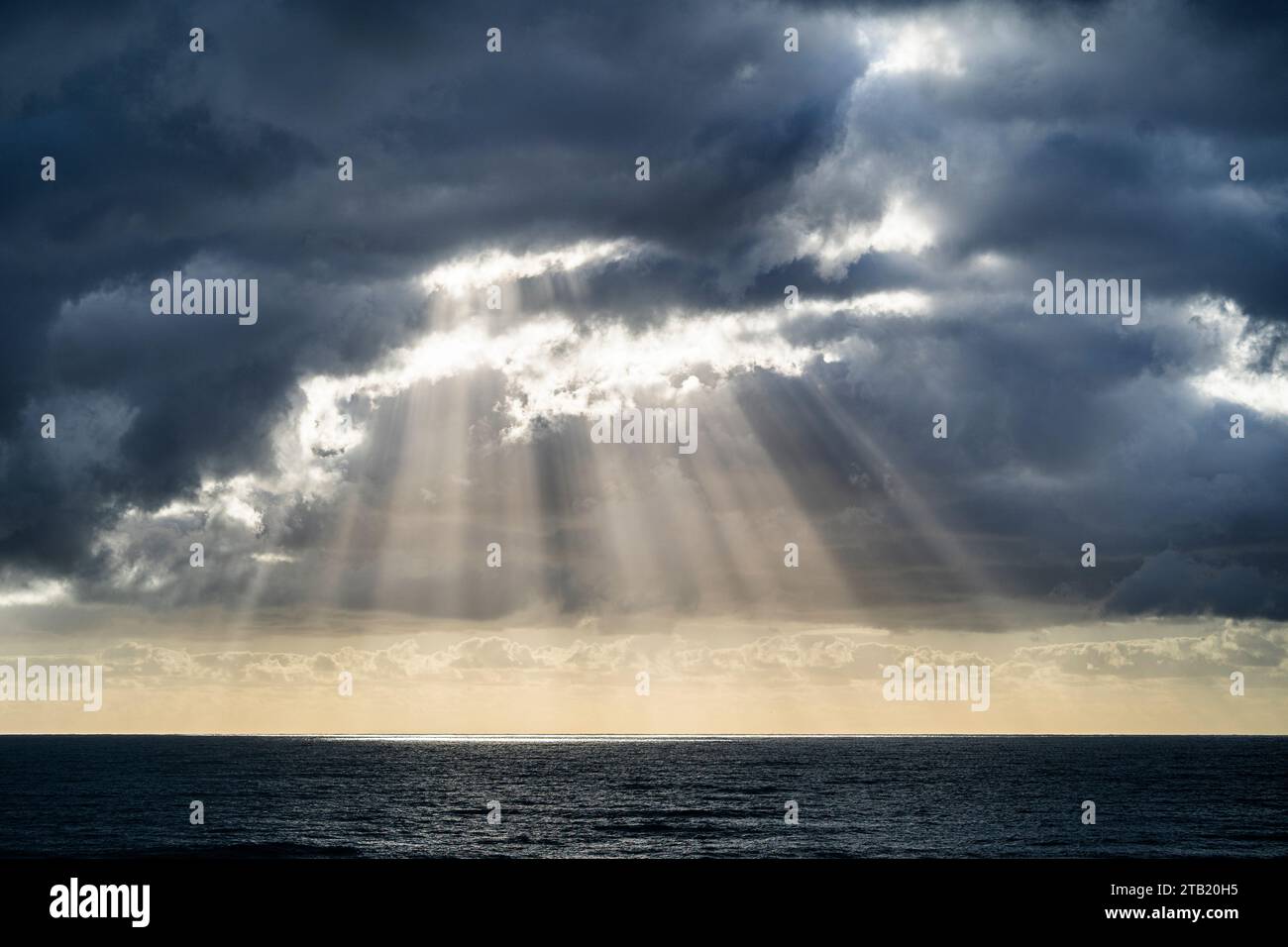 Rays of sun shining through storm clouds onto ocean Stock Photo - Alamy