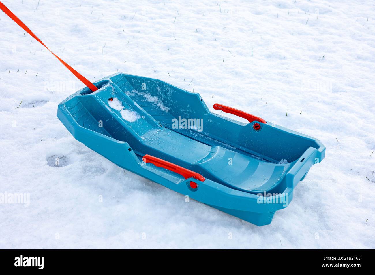 Empty blue plastic sled with a red rope lies on a snow-covered ground ...