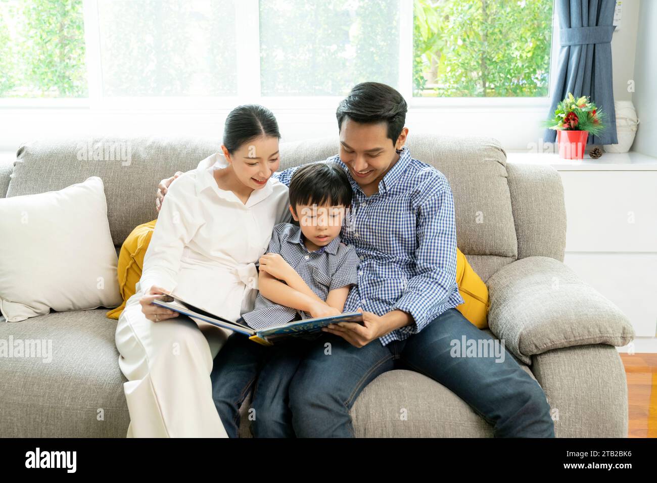 The parents and child read a book together in the living room Stock ...
